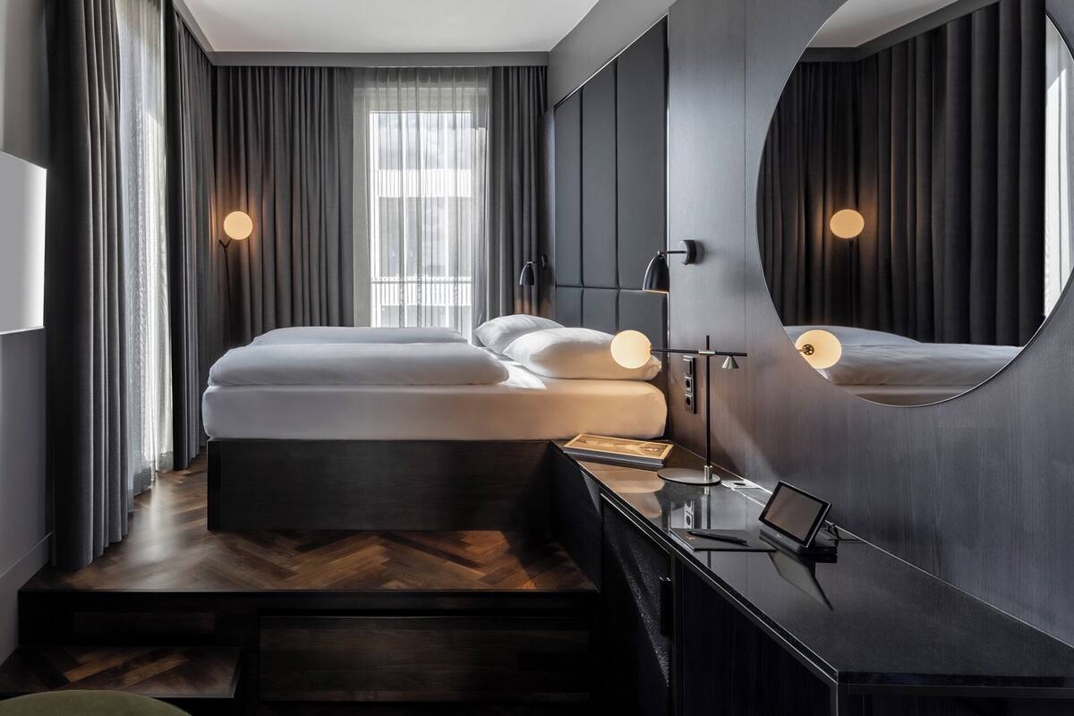 Quarto de hotel moderno com uma cama grande, uma escrivaninha com computador e um espelho amplo.