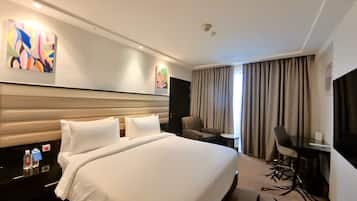 Quarto de hotel com uma cama grande, uma escrivaninha, uma cadeira e uma mesinha.