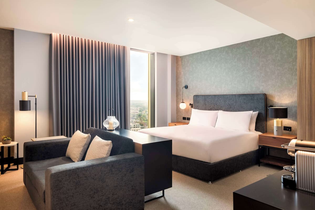 Quarto de hotel moderno com uma cama grande, um sofá, uma mesa de trabalho e vista para a cidade.