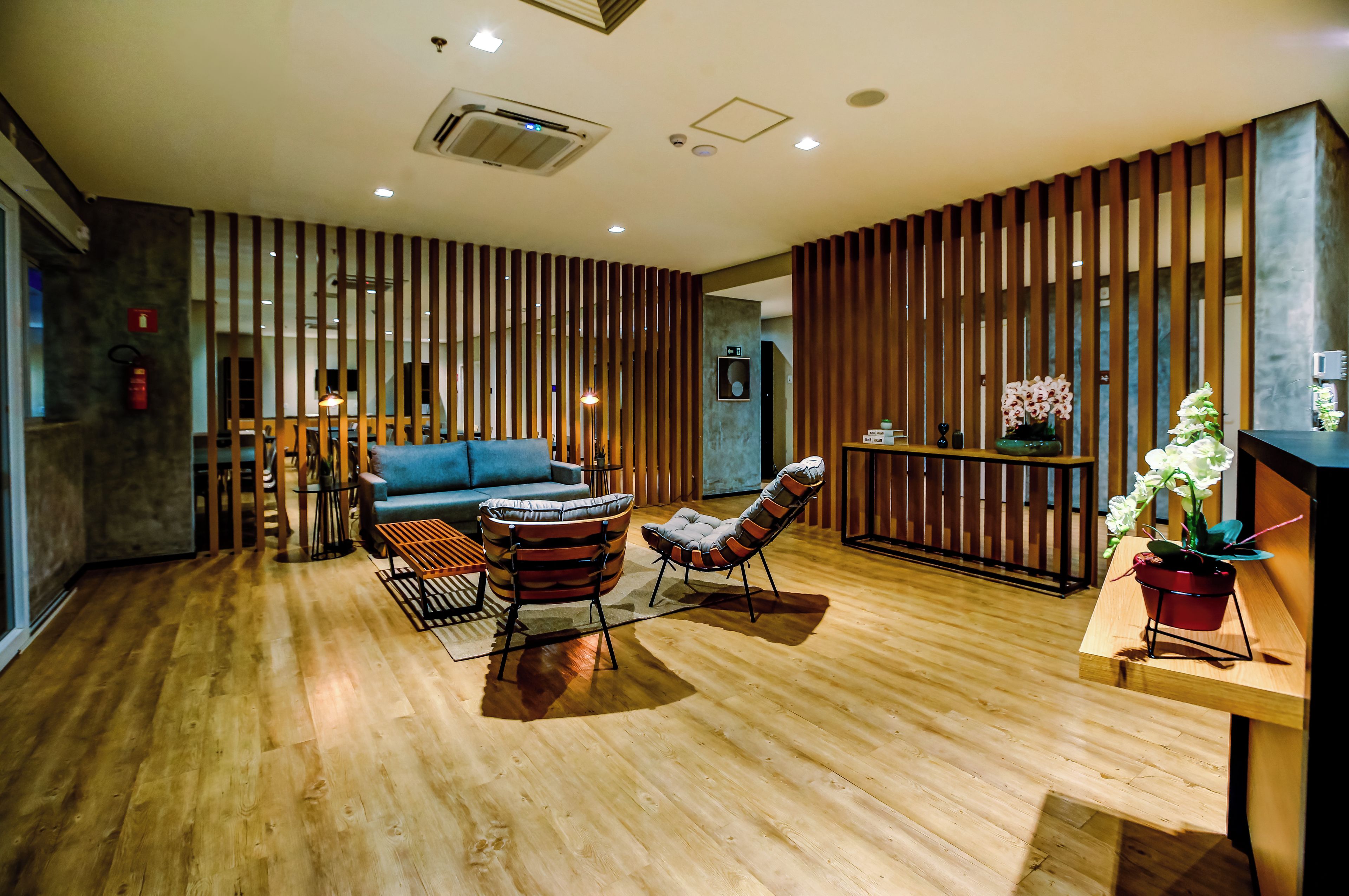 Interior moderno com piso de madeira, um sofá azul, poltronas listradas e um divisório de madeira.