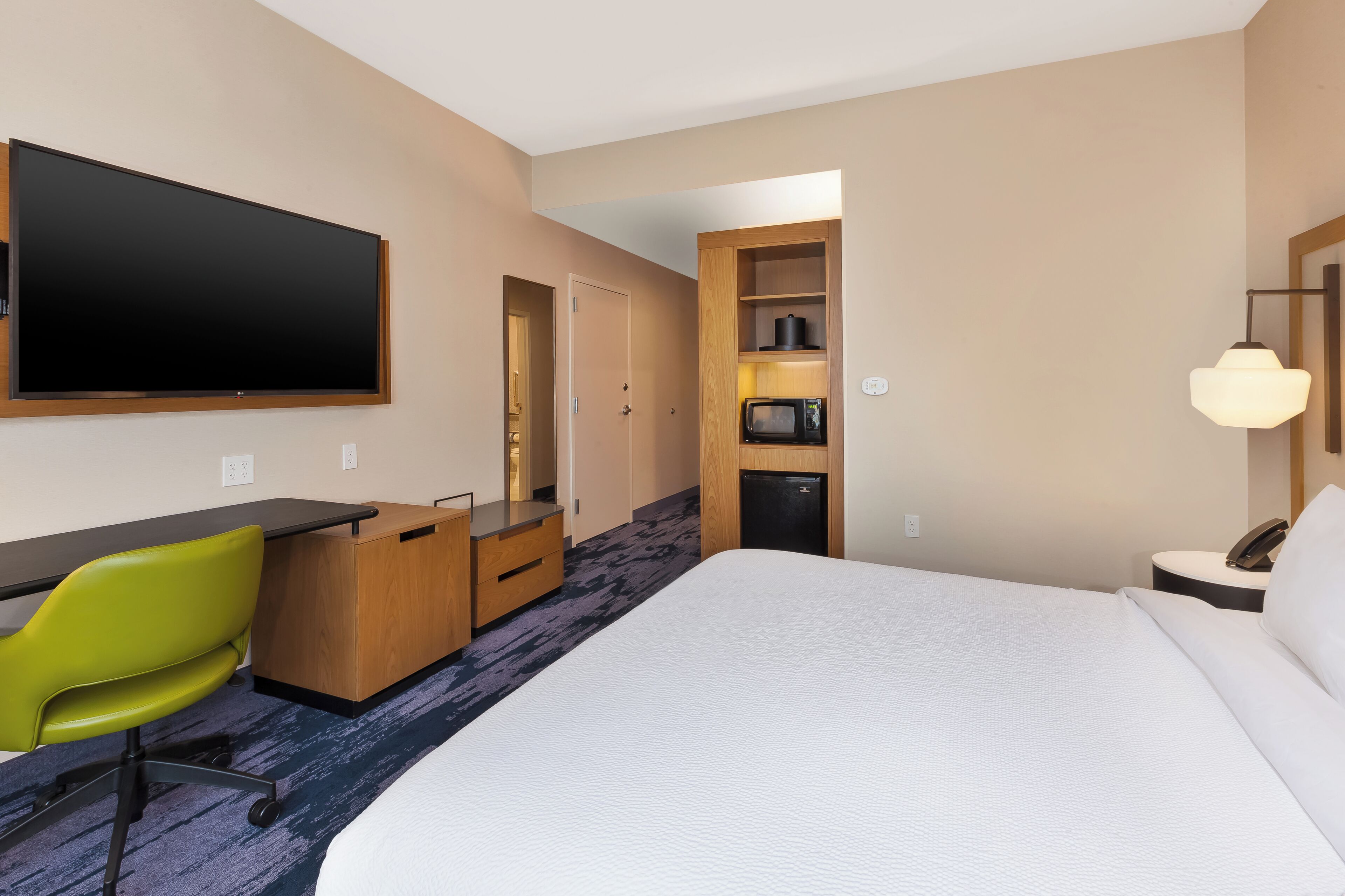 Quarto de hotel com cama, escrivaninha, cadeira, televisão, micro-ondas e frigorífico.