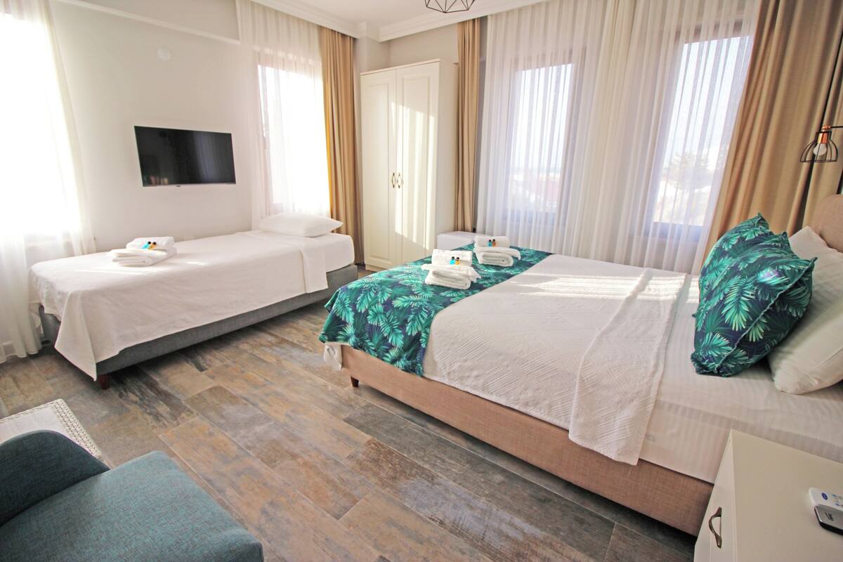Quarto de hotel com duas camas de solteiro, um sofá, uma televisão e um guarda-roupa.