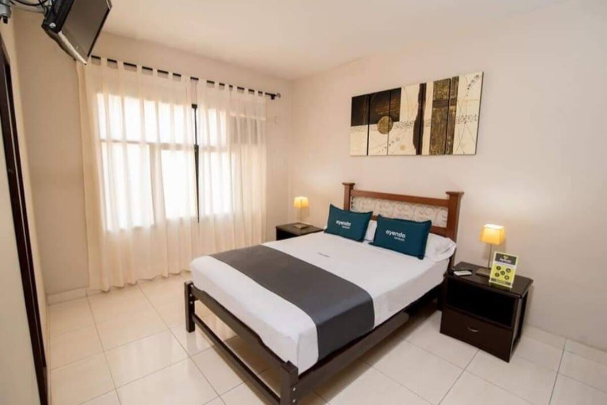 Quarto de hotel bem arrumado com cama, duas mesas de cabeceira e uma janela com cortinas.