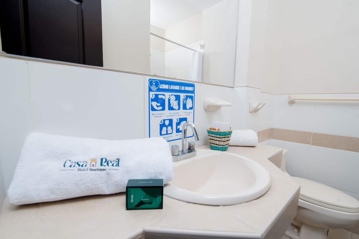 Casa de banho com lavatório, toalha, dispensador de sabonete e um aviso com instruções para lavar as mãos.