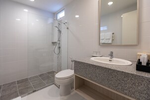 Uma casa de banho moderna com chuveiro, sanita, lavatório e um espelho grande.