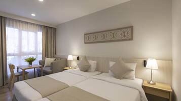 Quarto de hotel com uma cama grande, uma secretária e uma cadeira. Há uma janela com cortinas, uma obra de arte na parede e uma mesa de cabeceira com um abajur.