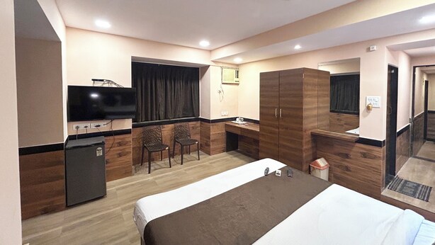 Quarto de hotel com cama, escrivaninha com cadeira, televisão e guarda-roupa.