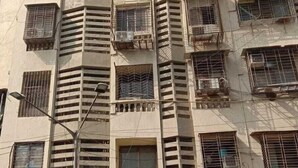 Edifício de vários andares com varandas, aparelhos de ar condicionado e uma rua na frente.