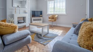 Uma sala de estar moderna com um sofá cinzento, uma mesa de centro, uma televisão e uma lareira.