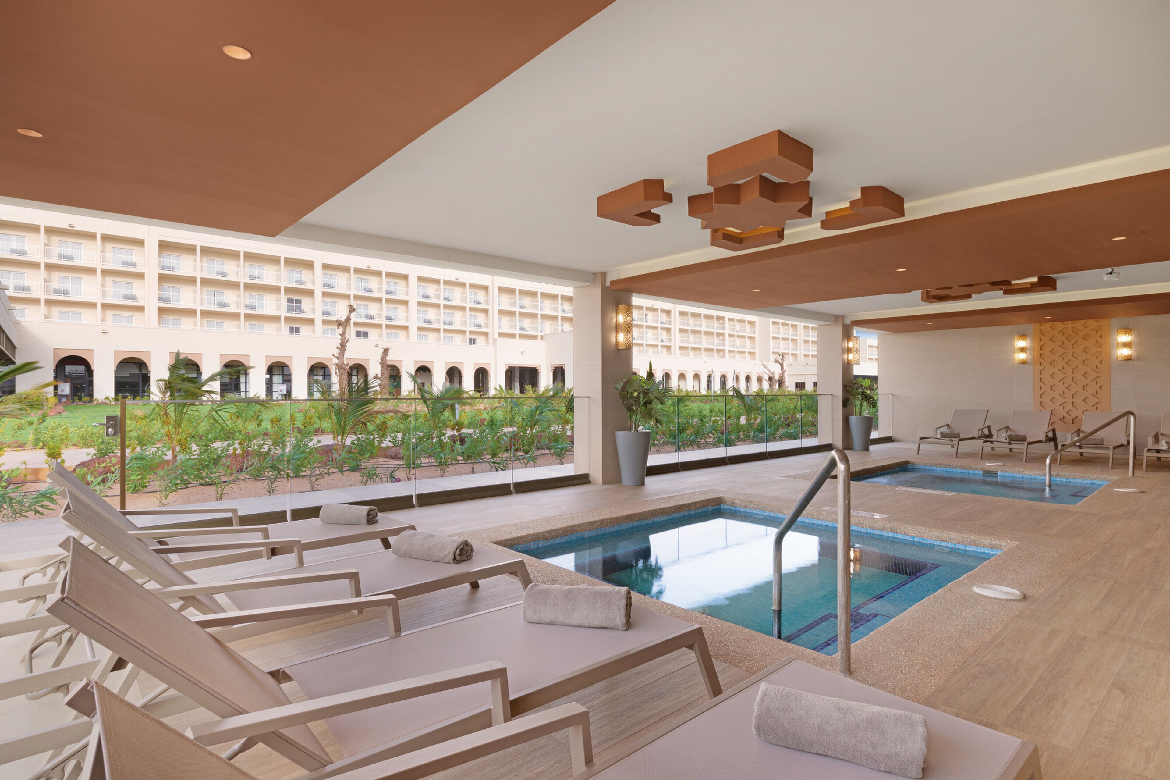 Uma área de piscina de hotel com espreguiçadeiras, uma piscina pequena e vista para a fachada do edifício.