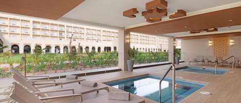 Uma área de piscina de hotel com espreguiçadeiras, uma piscina pequena e vista para a fachada do edifício.