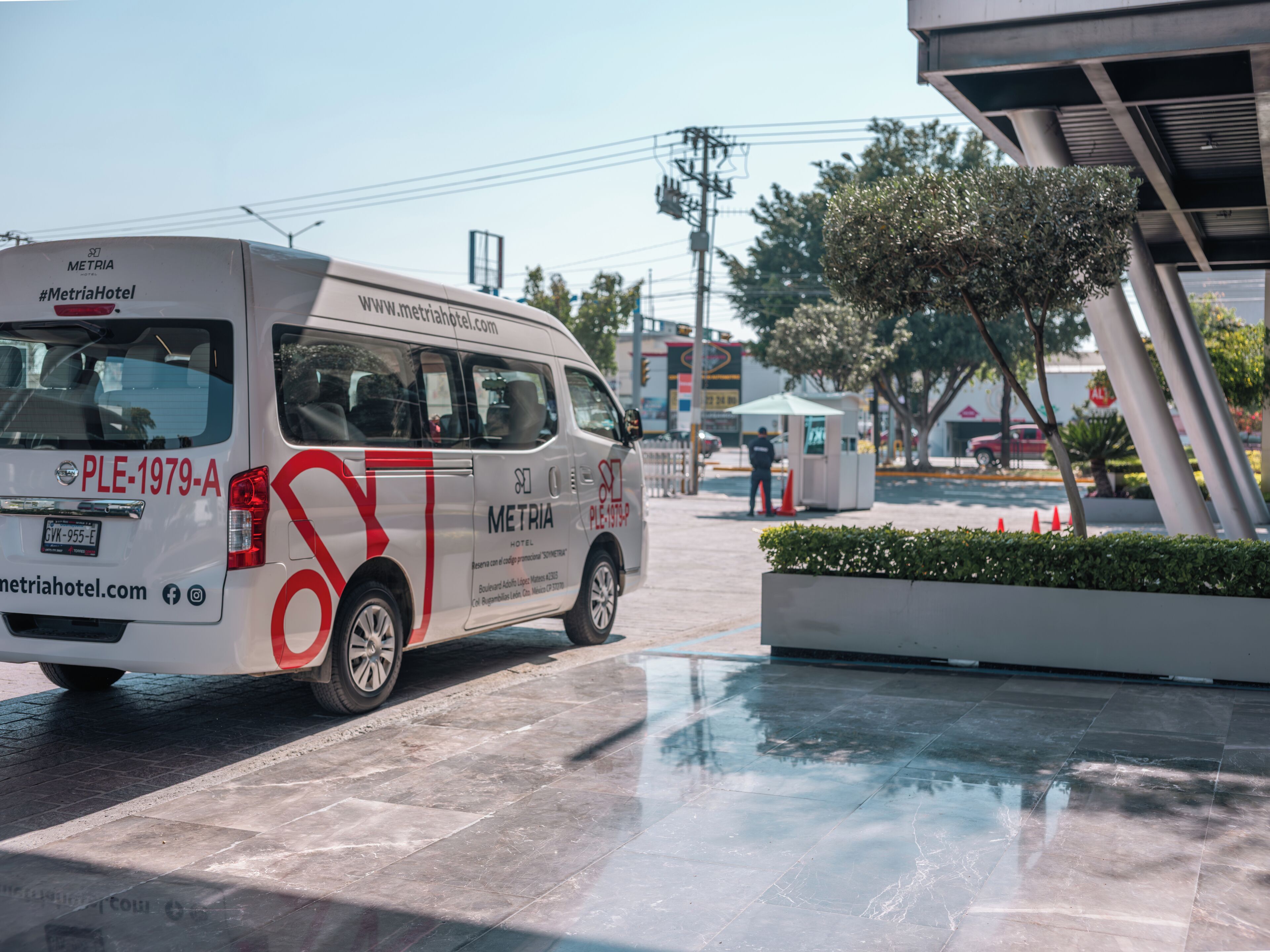 Uma carrinha branca com detalhes vermelhos e a marca METRIA HOTEL estacionada em pavimento molhado.