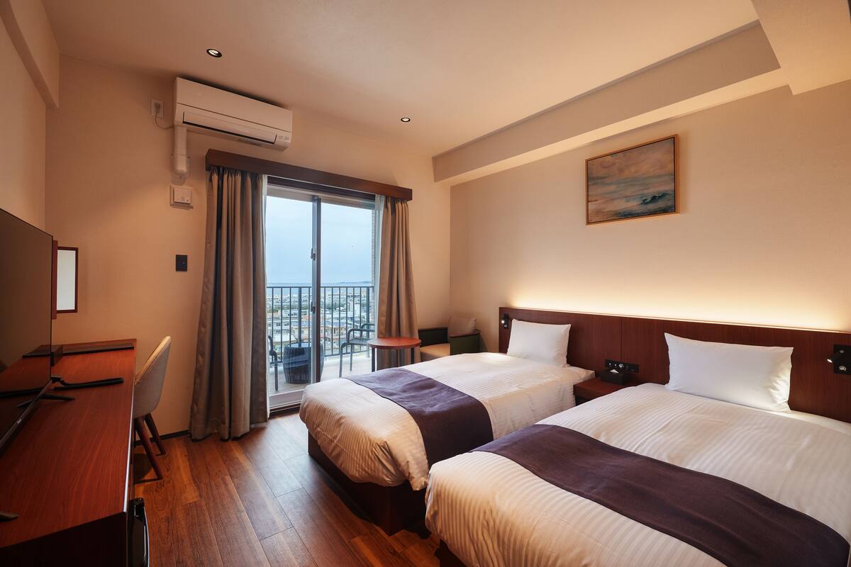 Quarto de hotel com duas camas, uma escrivaninha e varanda com vista.
