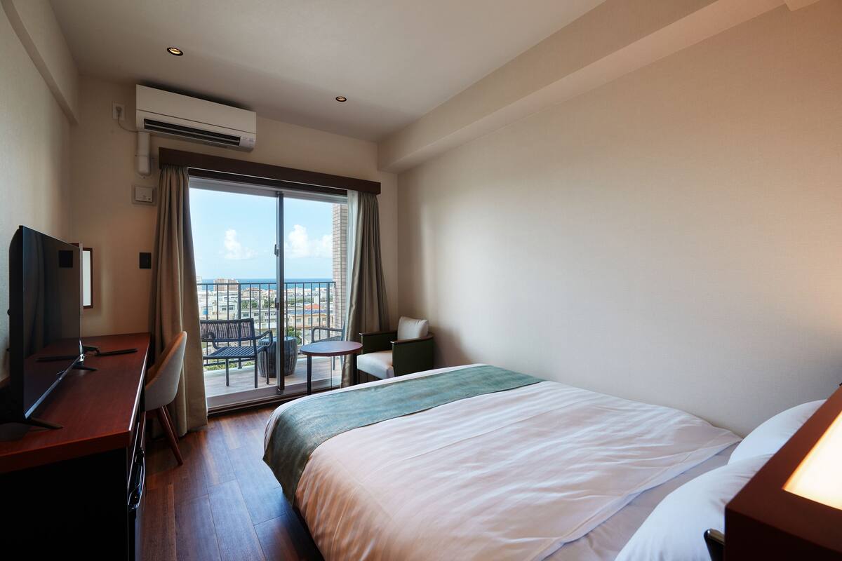 Quarto de hotel com cama, escrivaninha, cadeira, mesinha e varanda com vista.