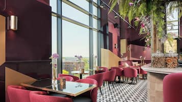 Um restaurante moderno com cadeiras vermelhas, piso com padrão preto e branco e grandes janelas com vista para a cidade.