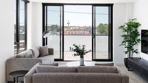 Uma sala de estar moderna com um sofá modular cinza, uma mesinha redonda e uma janela grande com vista para a cidade.