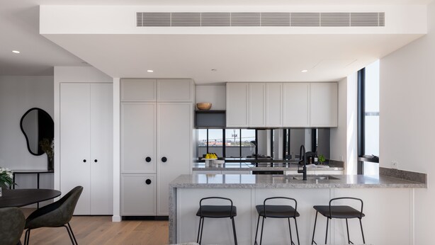 Cozinha moderna com ilha central, banquetas de bar e área de refeições com mesa redonda e cadeiras.