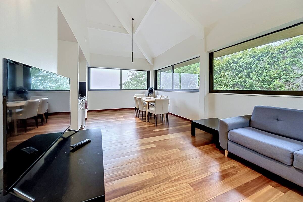 Uma sala moderna com sofá, área de jantar e janelas amplas.