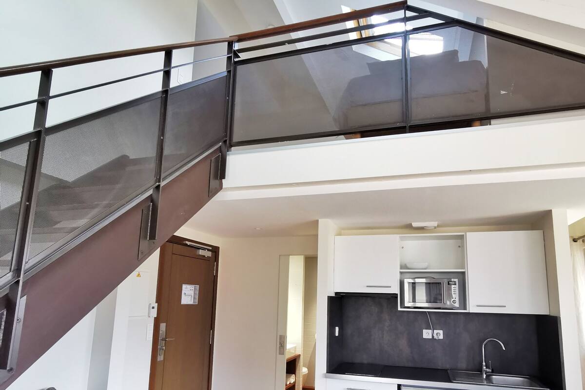 Um apartamento moderno com sala de estar, pequeno espaço de cozinha e escada com guarda-corrimão de vidro.