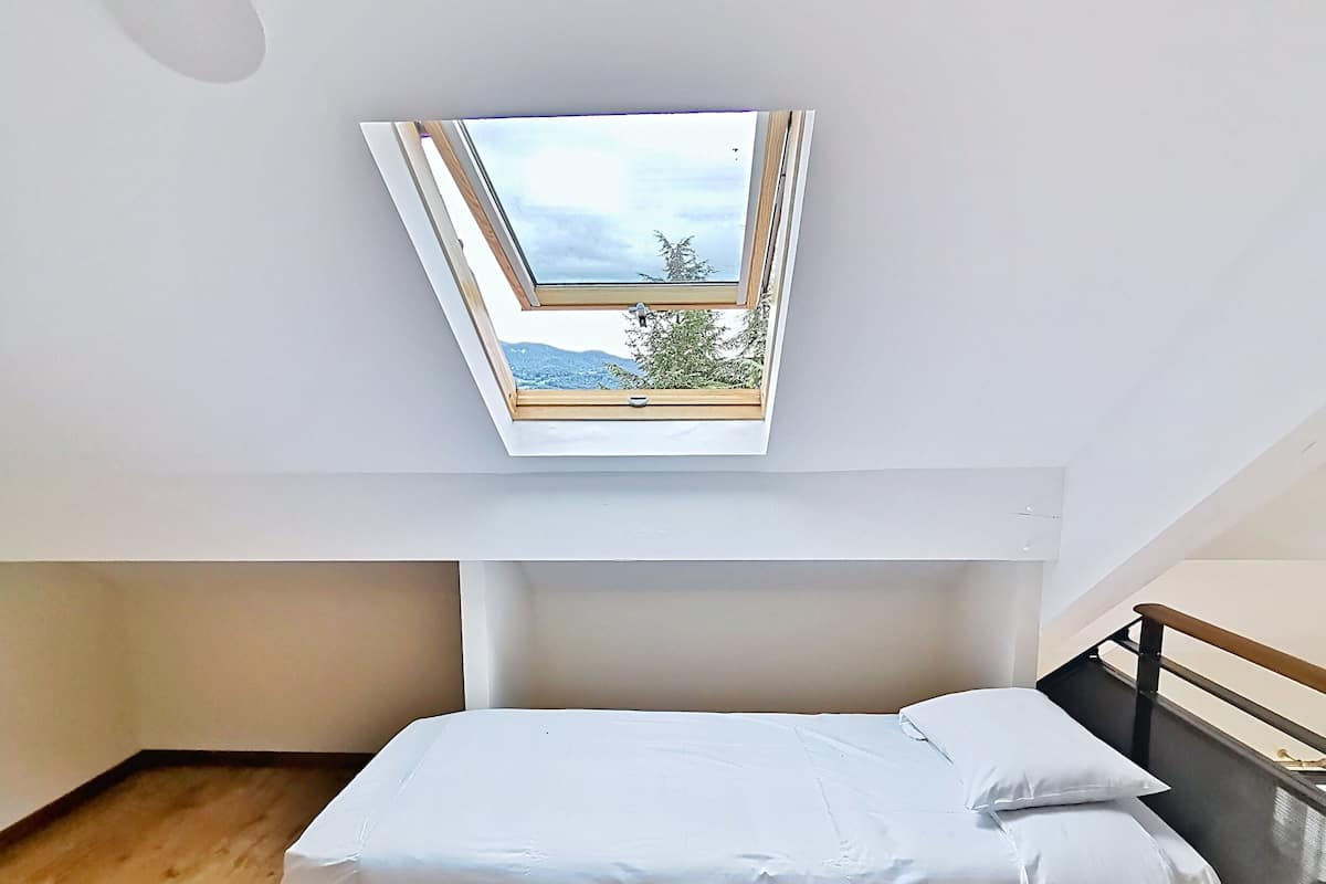 Quarto com claraboia, cama e vista para uma paisagem.