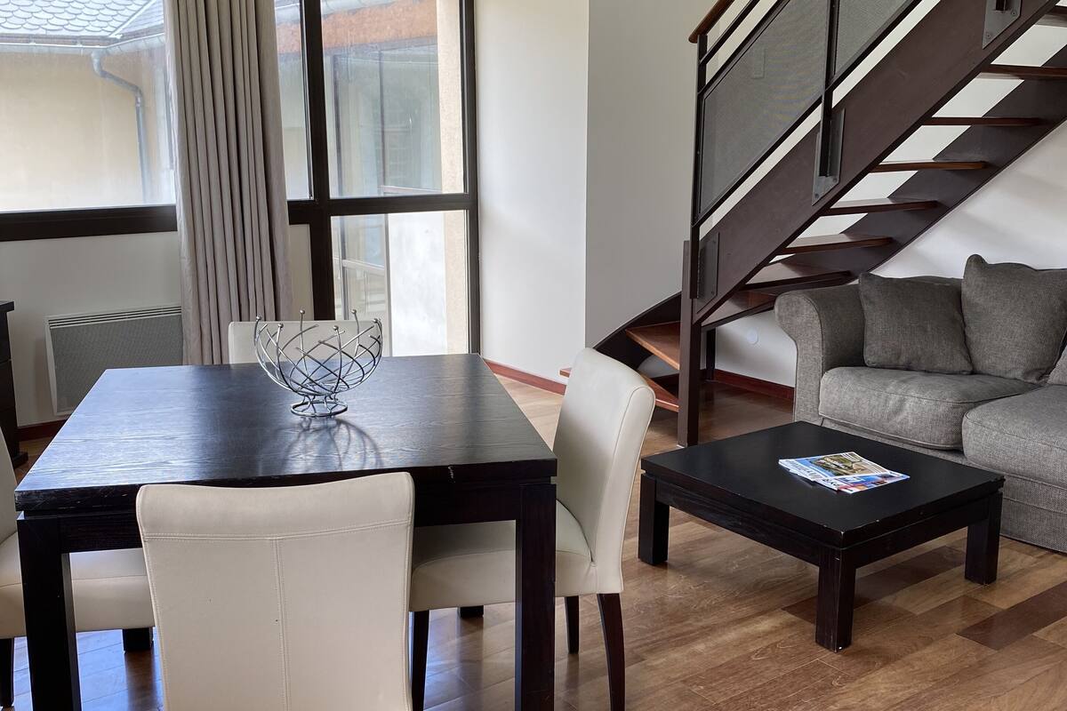 Uma sala de estar moderna com uma mesa de jantar, cadeiras, um sofá e uma escada.