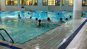 Piscina interna com várias pistas de natação, um tobogã aquático e piso revestido de azulejos.