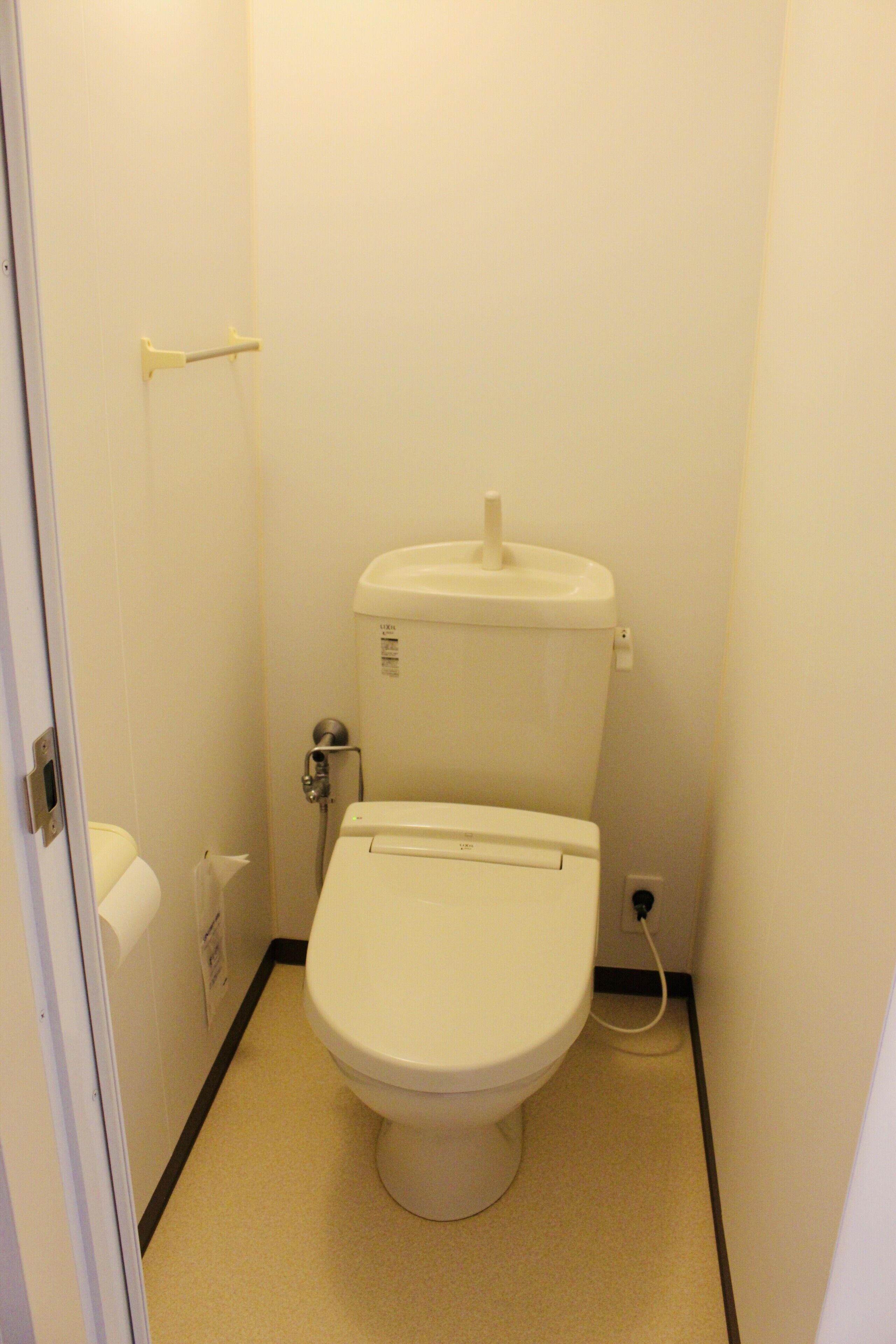 Casa de banho pequena e limpa, com sanita, suporte para toalhas e painel de controlo do chuveiro.