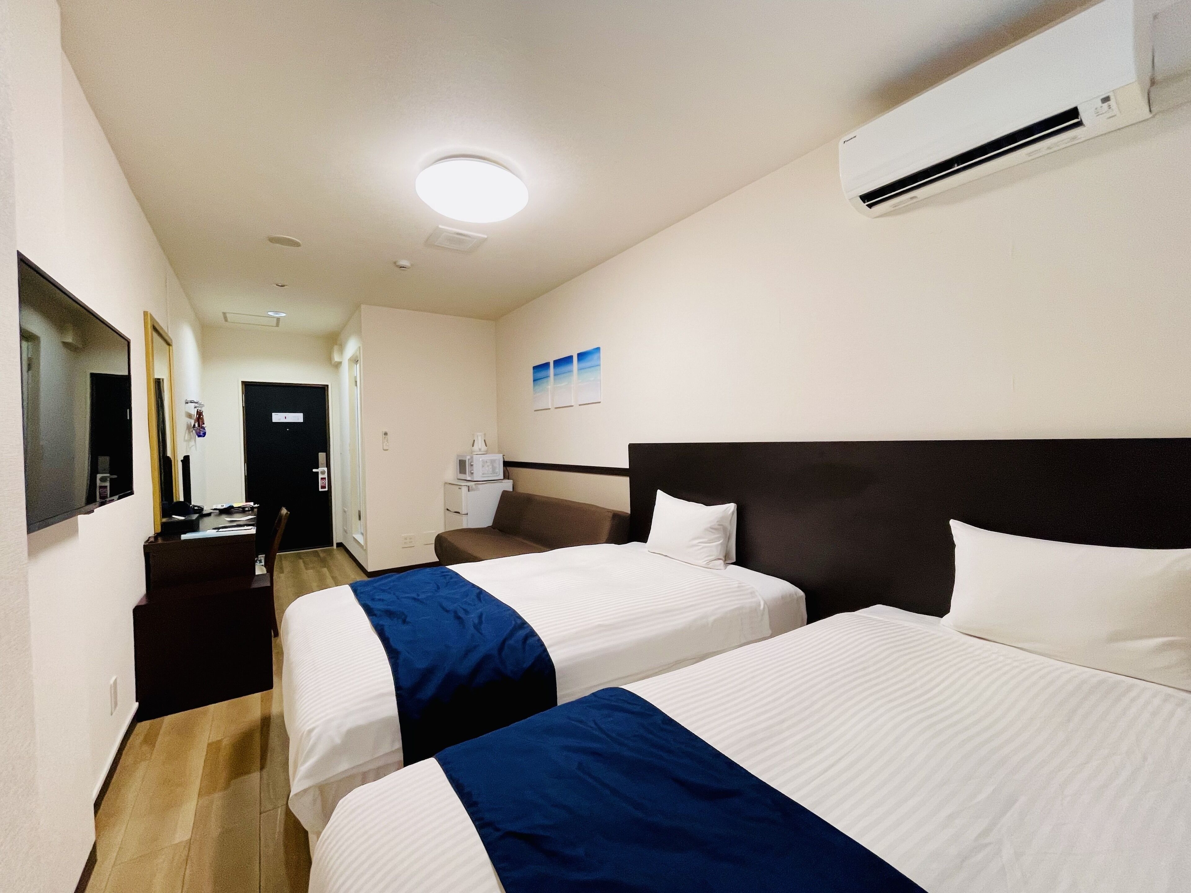 Quarto de hotel com duas camas, uma escrivaninha, uma cadeira, aparelho de ar condicionado e uma porta que dá para outro quarto.
