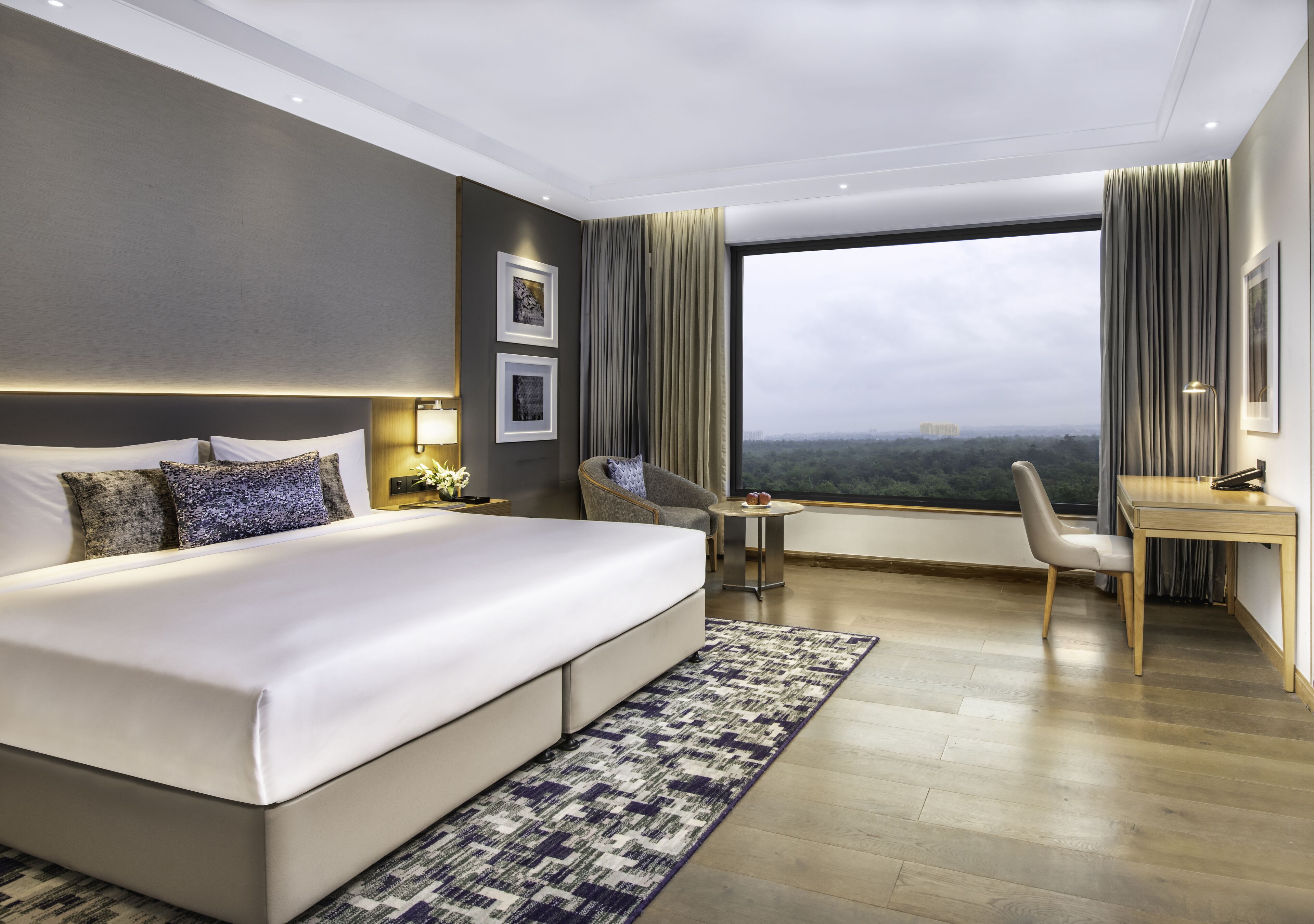 Quarto de hotel moderno com uma cama grande, uma escrivaninha e vista para a cidade.