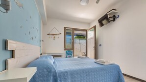 Quarto com cama, cadeira, escrivaninha, janela e porta que dá para o exterior.