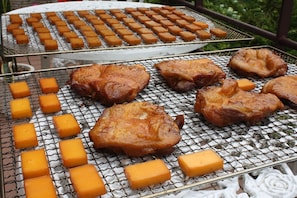 Uma churrasqueira com diversos tipos de carne e queijo sendo preparados ao ar livre.