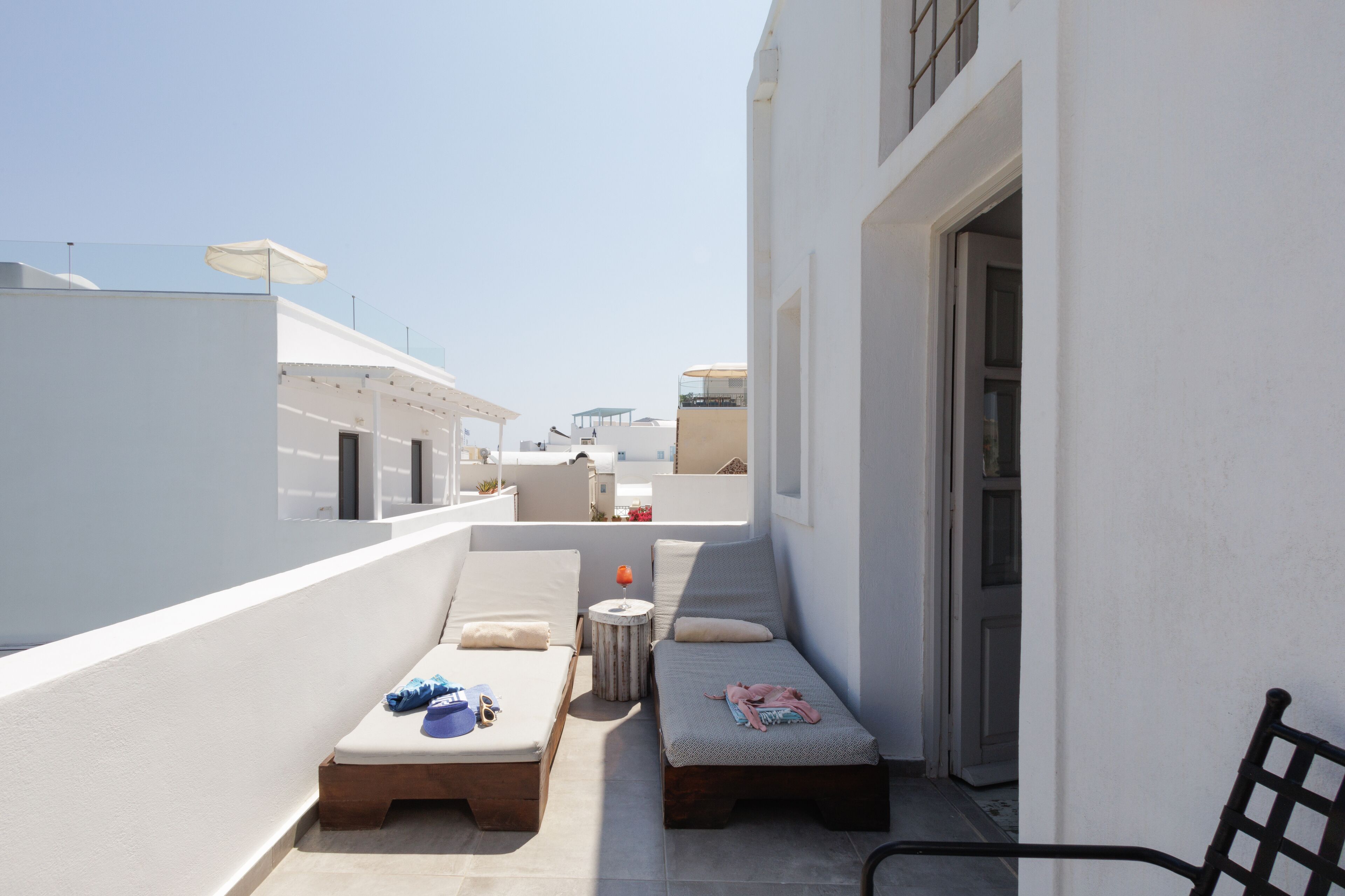 Terraço no telhado com duas espreguiçadeiras, uma mesa redonda pequena com uma bebida e vista para a paisagem urbana.