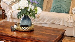 Uma sala de estar com uma mesa de centro de madeira, um vaso com flores brancas e um controle remoto sobre a mesa.