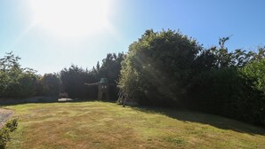 Uma área externa com gramado, uma grande árvore e uma estrutura com telhado verde.