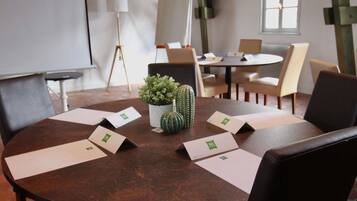 Uma sala de conferências com uma mesa redonda, cadeiras, um quadro branco e um vaso de planta.