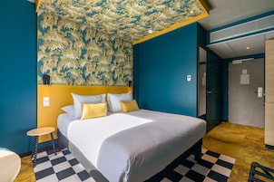 Quarto de hotel com cama, uma mesa redonda pequena, tapete xadrez e teto estampado.