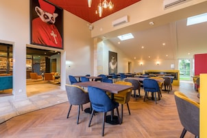Uma ampla área de refeições com várias mesas e cadeiras, um grande mural na parede e vista para o exterior.