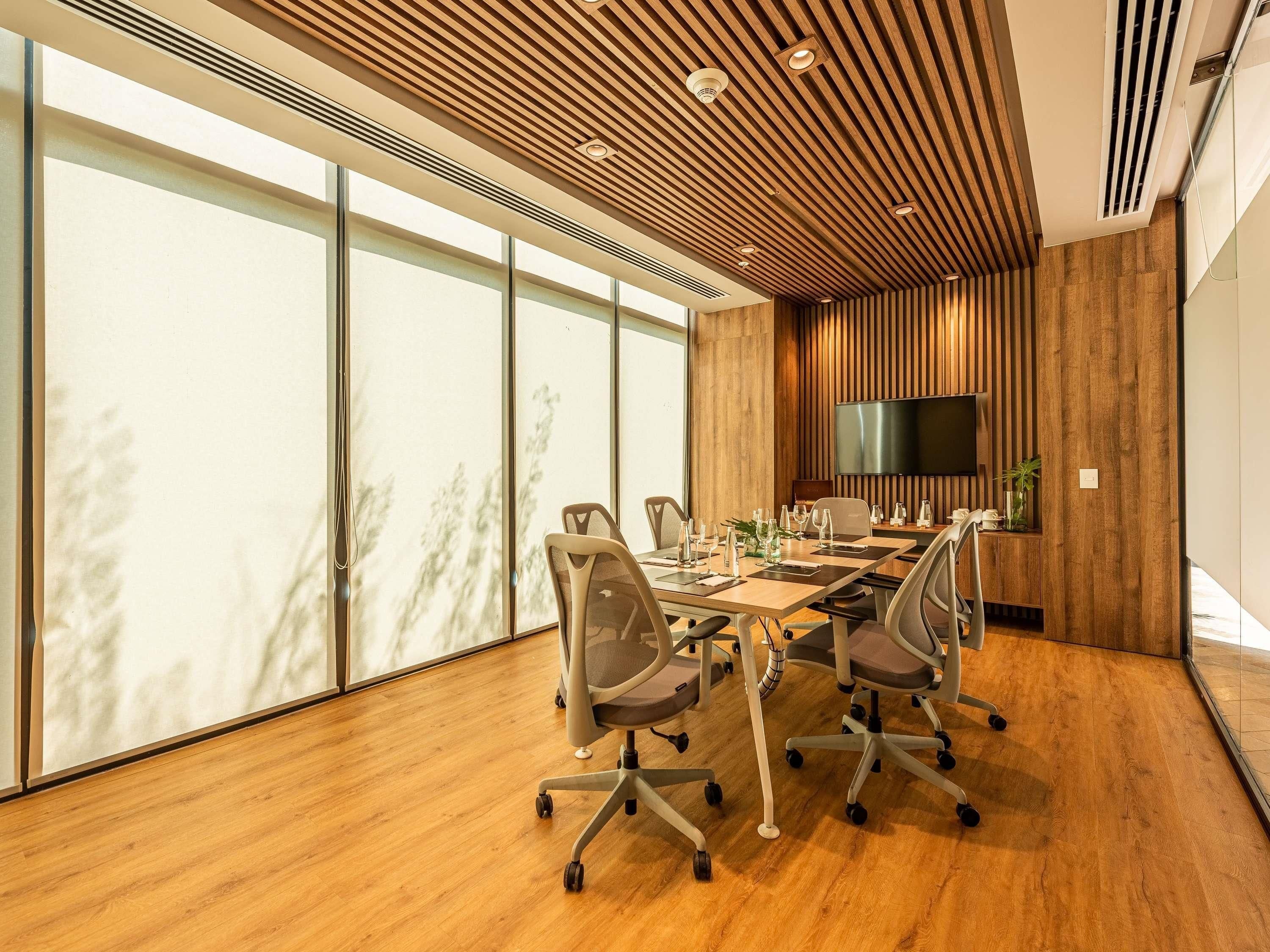 Uma sala de conferências com uma mesa comprida, cadeiras, uma TV e teto de madeira.