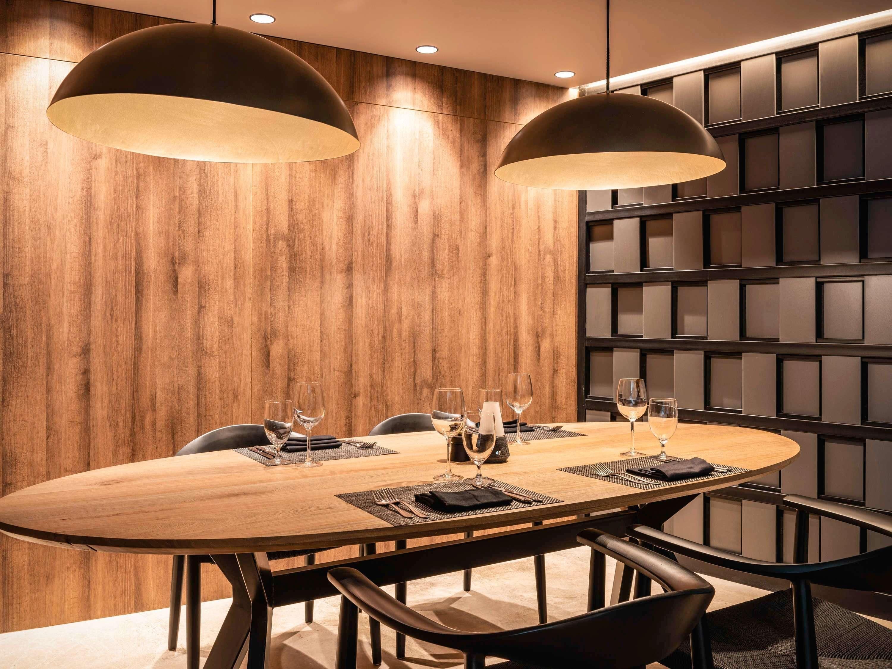 Uma sala de jantar moderna com mesa de madeira, cadeiras pretas e iluminação pendente.
