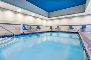 Piscina interna com água azul cristalina, rodeada por cadeiras azuis e uma parede revestida com um bordado azul.