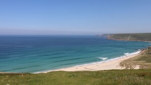 Paisagem costeira com praia, áreas gramadas e céu azul límpido.