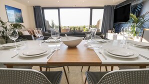 Uma área de refeições com uma mesa posta para quatro pessoas, rodeada por cadeiras, com vista para o exterior.