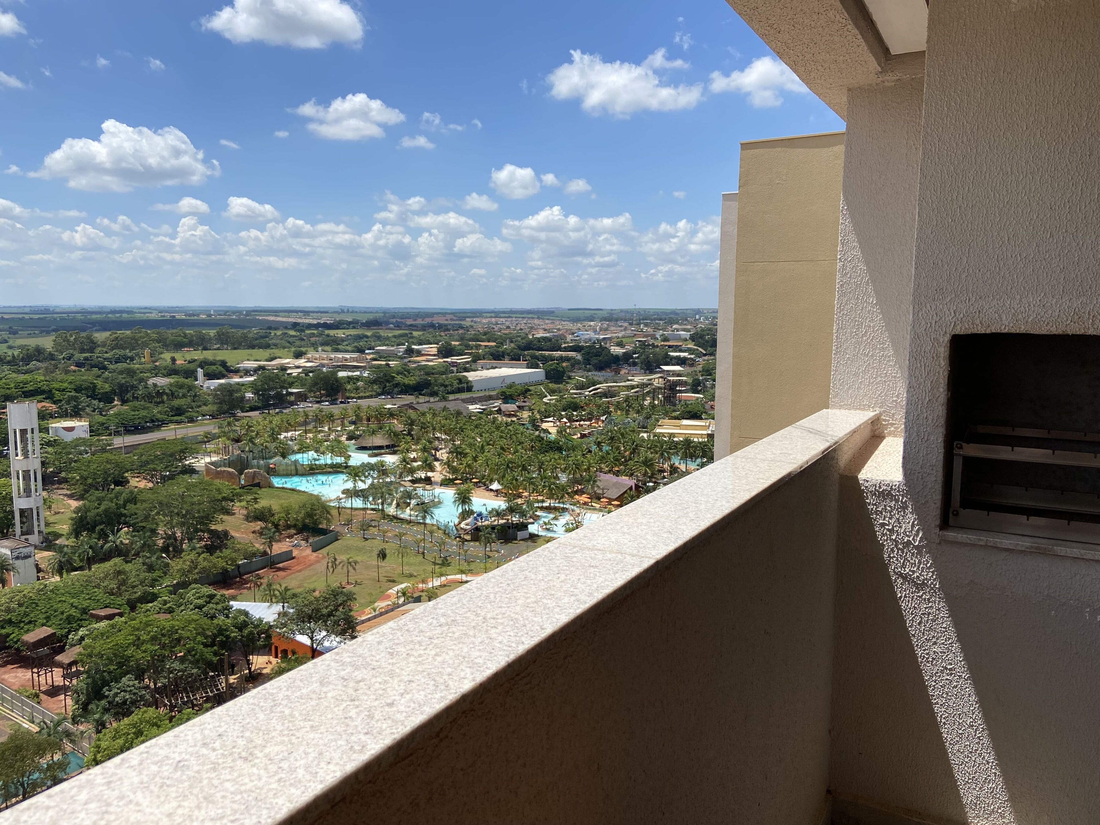 Vista de uma varanda com vista para um resort com várias piscinas, vegetação exuberante e edifícios ao longe.