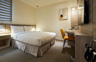 Quarto de hotel com uma cama, uma escrivaninha, uma cadeira, um espelho e um quadro na parede.