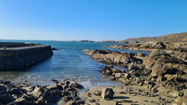 Uma área costeira rochosa com um cais de pedra que se estende para o mar.