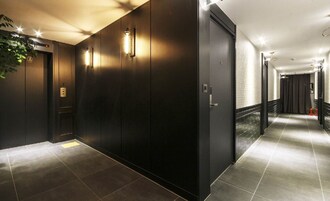 Corredor moderno de hotel com paredes escuras, iluminação embutida e piso ladrilhado.