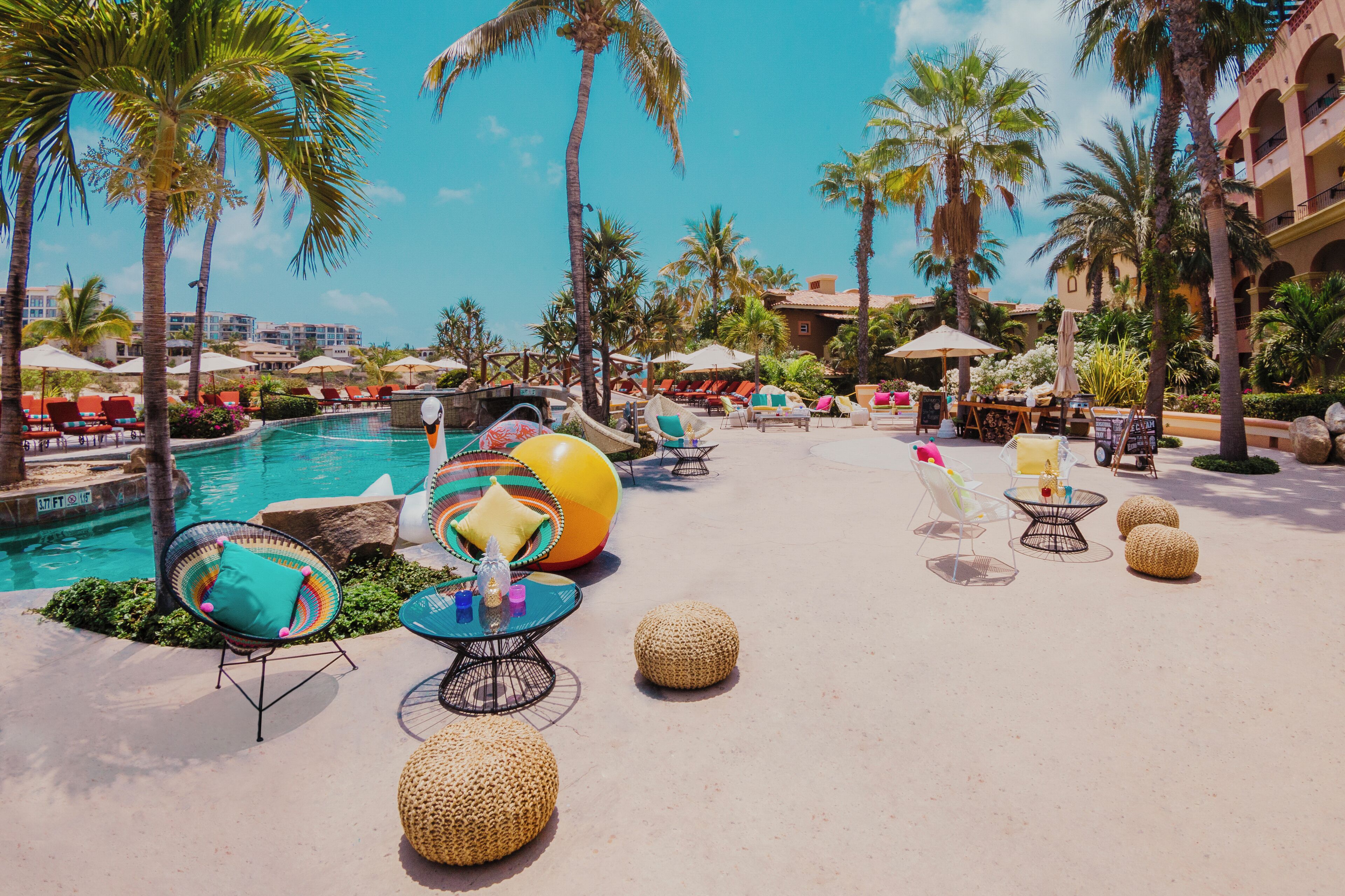Área de piscina em resort com espreguiçadeiras, hidromassagem e palmeiras.