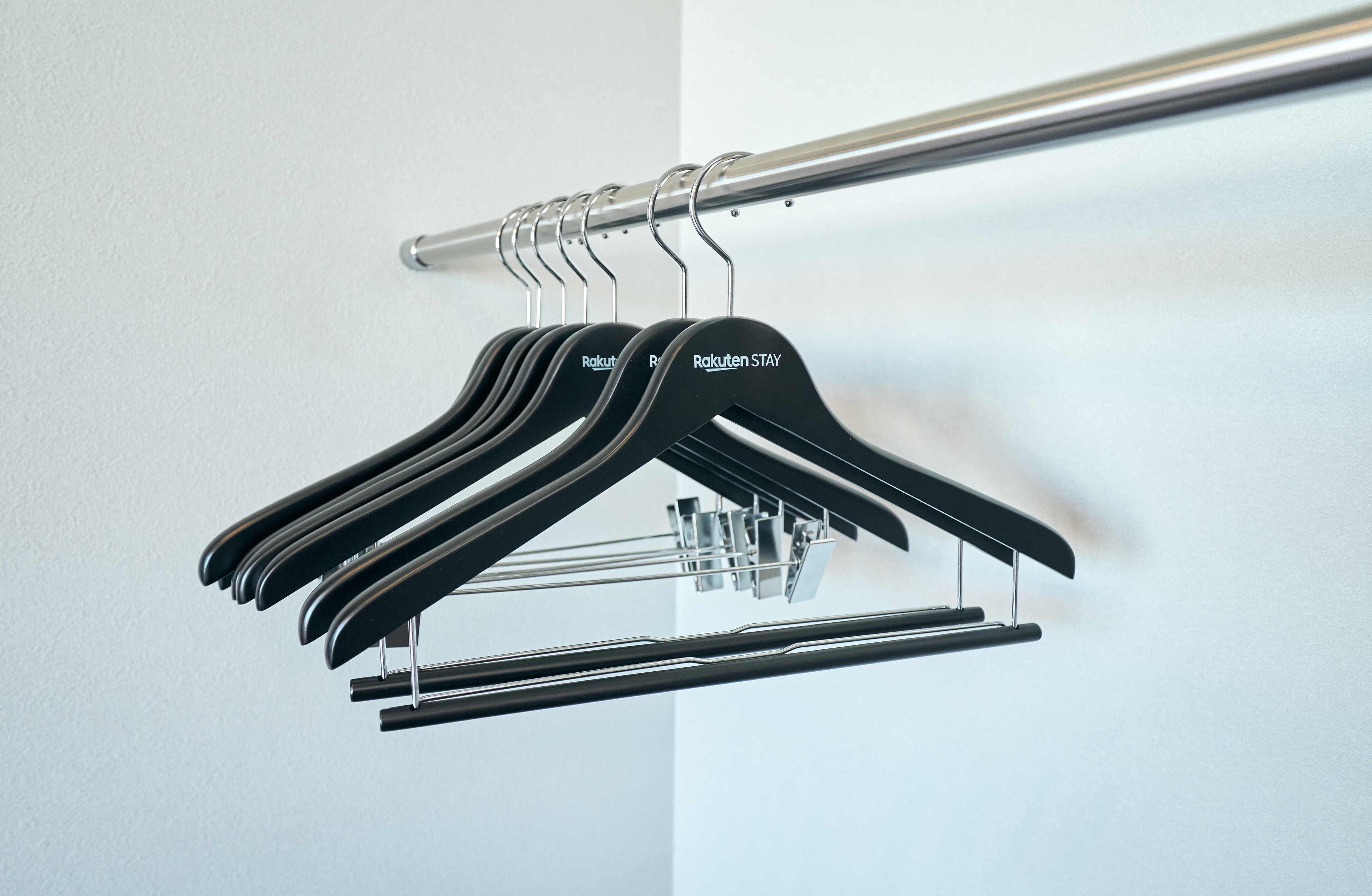 Uma estante de metal com vários cabides pretos identificados como "Rakuten STAY" em frente a uma parede branca.