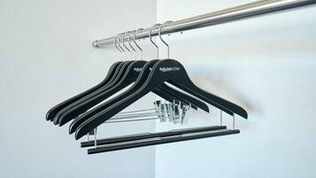 Uma estante de metal com vários cabides pretos identificados como "Rakuten STAY" em frente a uma parede branca.