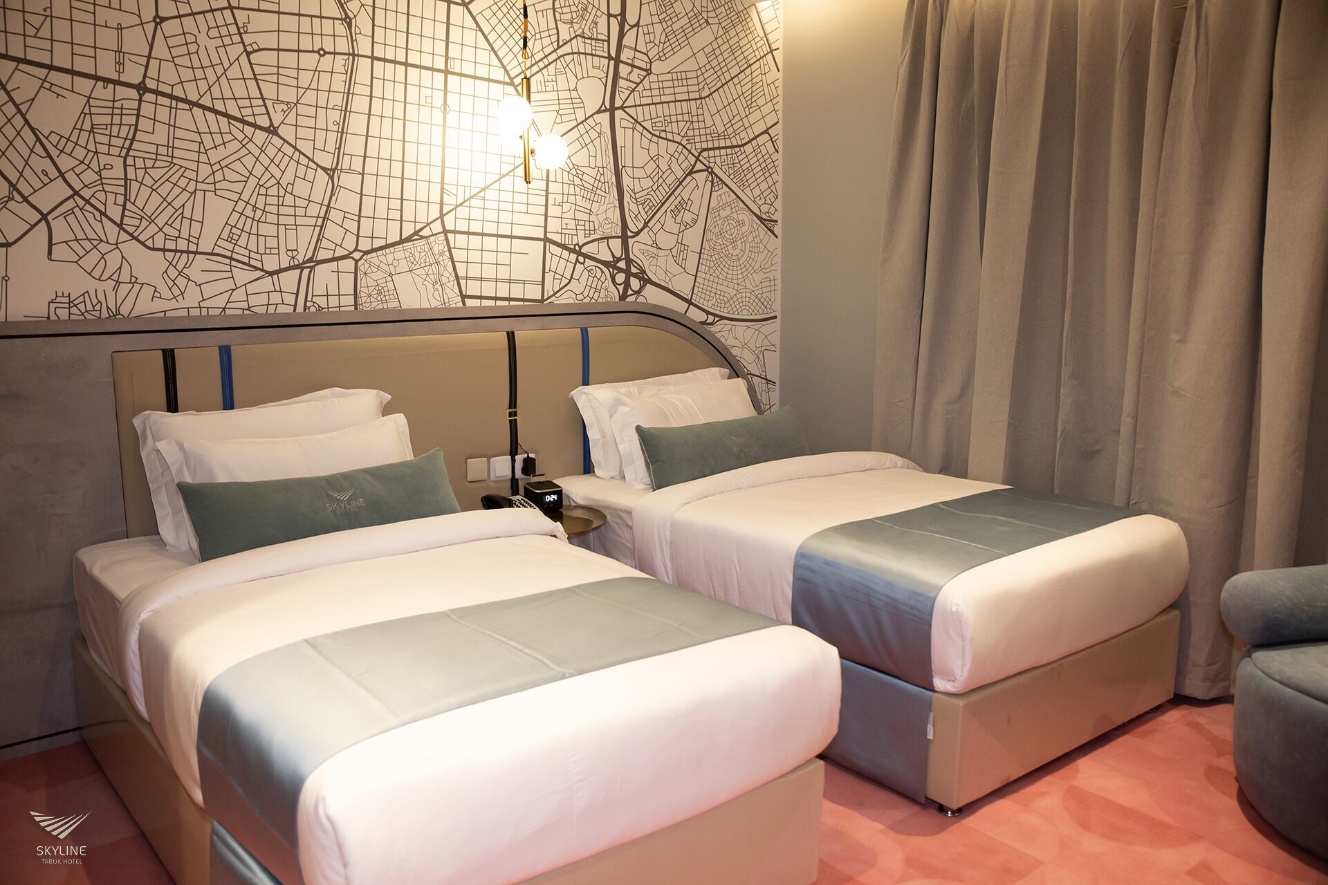 Quarto de hotel com duas camas, um mural de mapa, uma escrivaninha e uma cadeira.